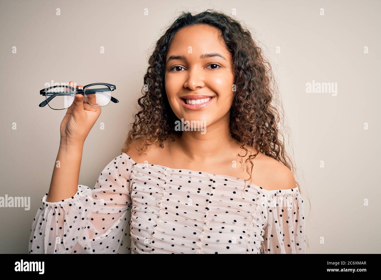 Young beautiful optical woman with curly hair holding vision glasses ...