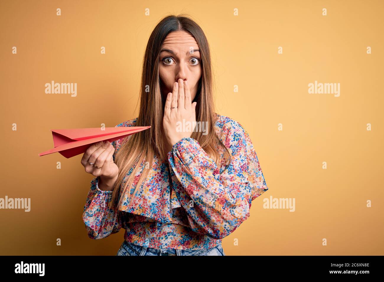 Young blonde woman holding paper plane over yellow isolated background ...