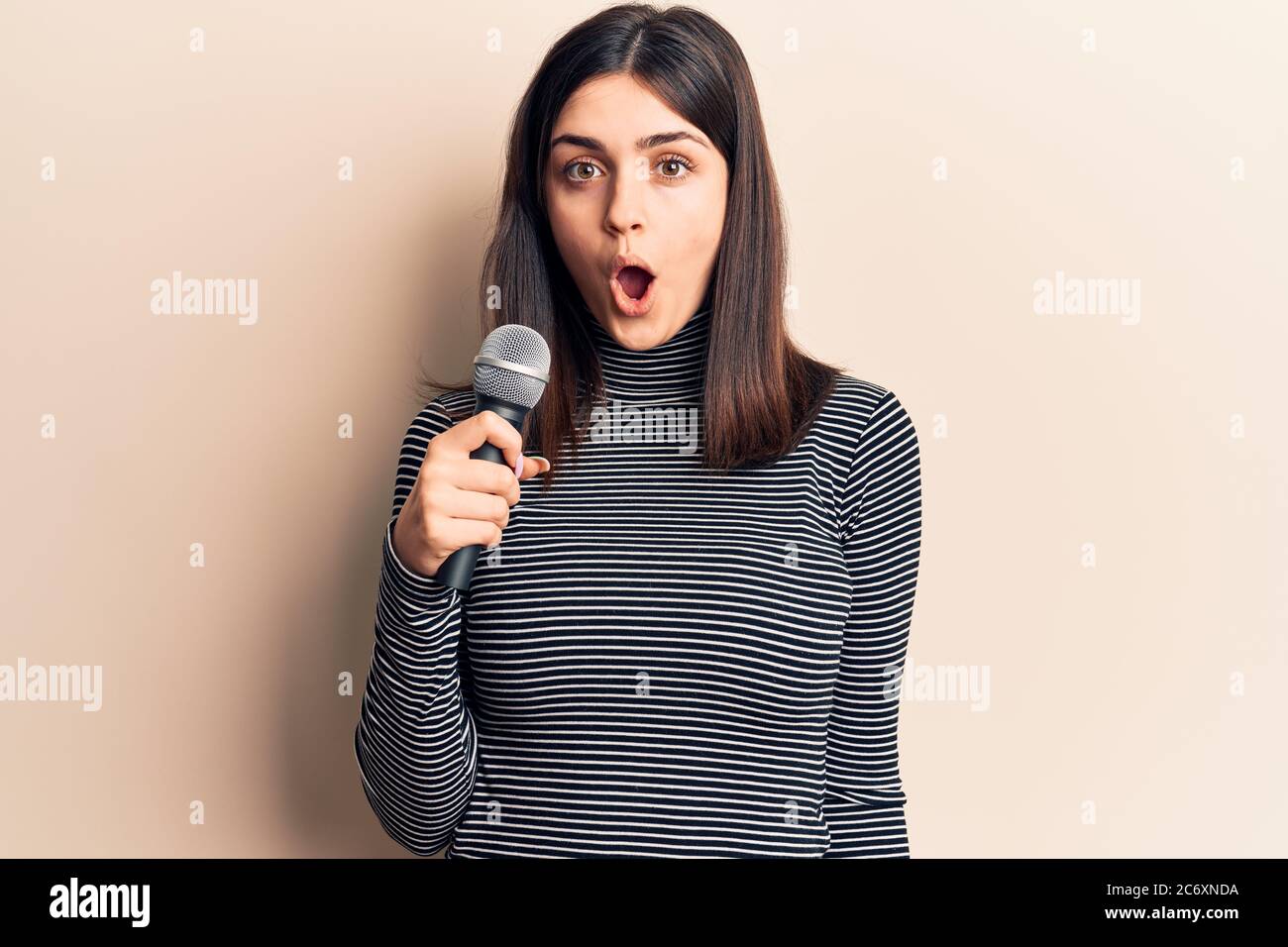 Young beautiful girl singing song using microphone scared and amazed ...