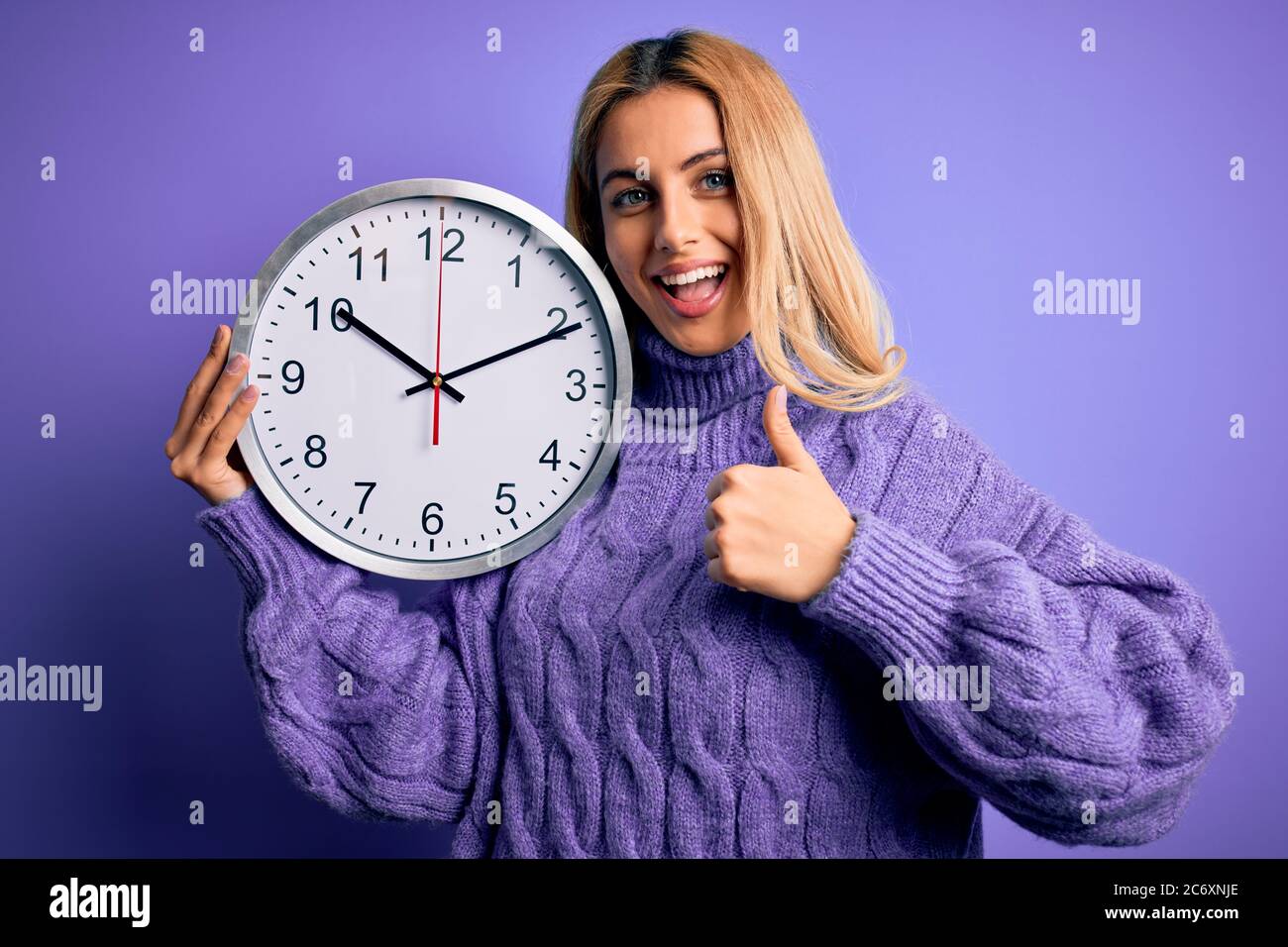 Young beautiful blonde woman doing countdown holding big clock over ...