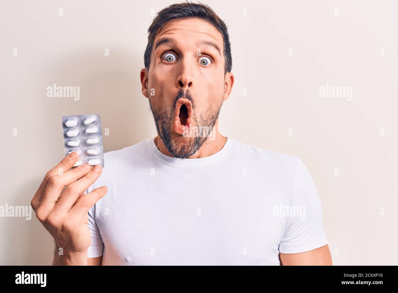 Young handsome man holding medicine pills standing over isolated white ...