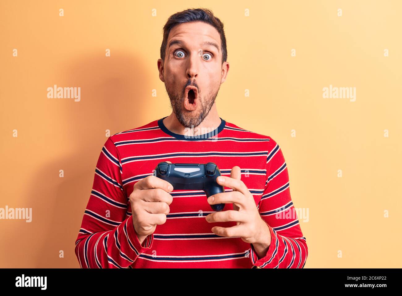 Young handsome gamer man playing video game using gamepad over yellow ...