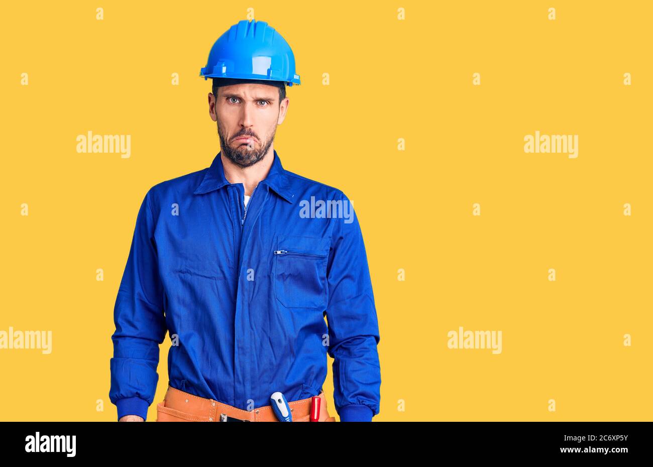 Young handsome man wearing worker uniform and hardhat crazy and scared ...