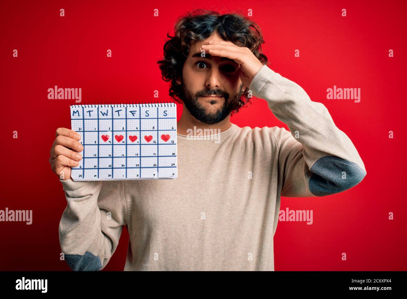 Young handsome man with beard holding calendar over isolated red ...