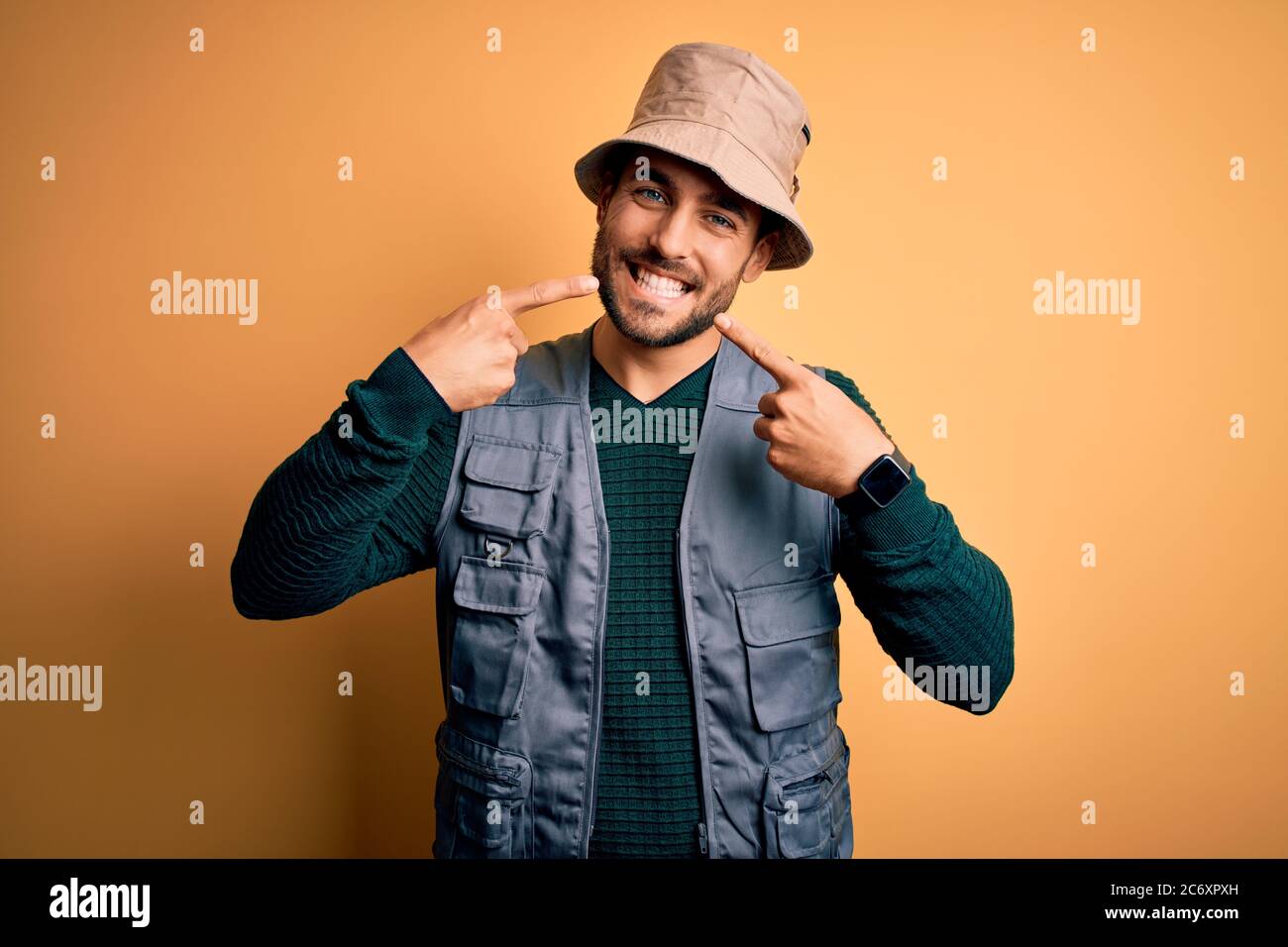 Handsome tourist man with beard on vacation wearing explorer hat over ...