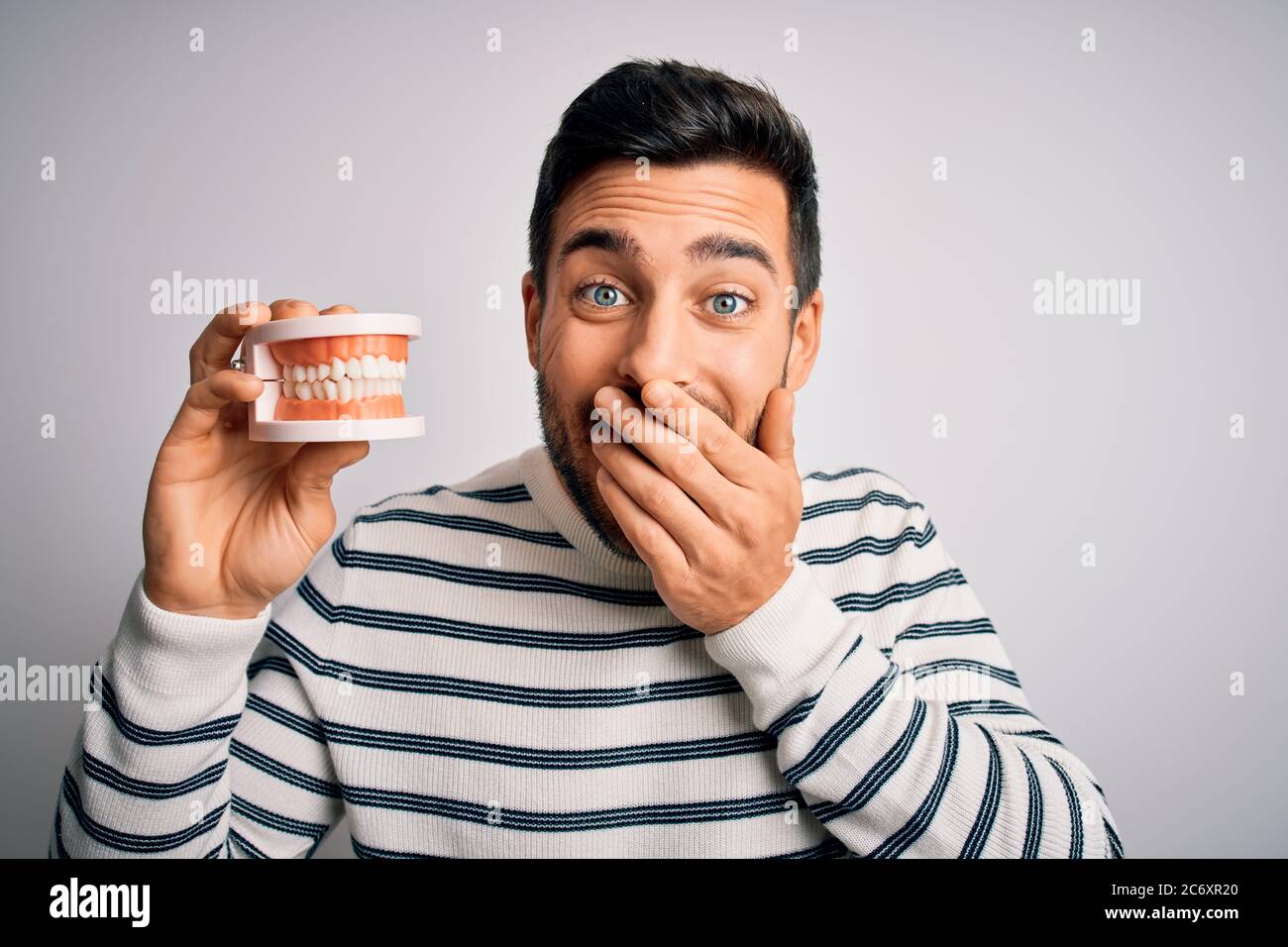 Young handsome man with beard holding plastic denture teeth over white ...