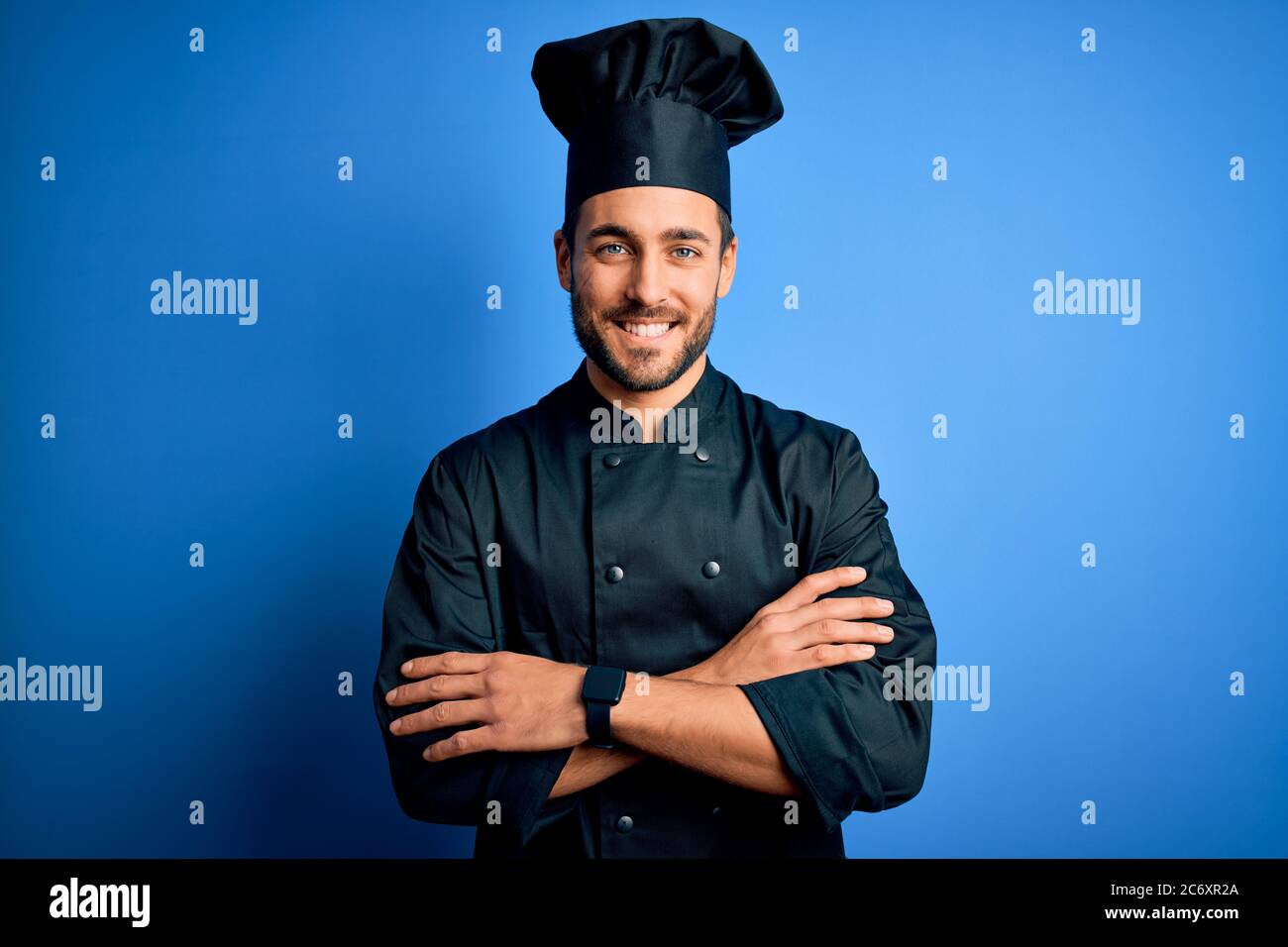 Young handsome chef man with beard wearing cooker uniform and hat over ...