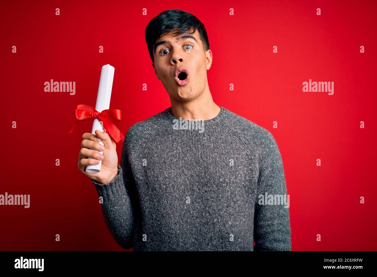 Young student man holding university graduated diploma degree over red ...