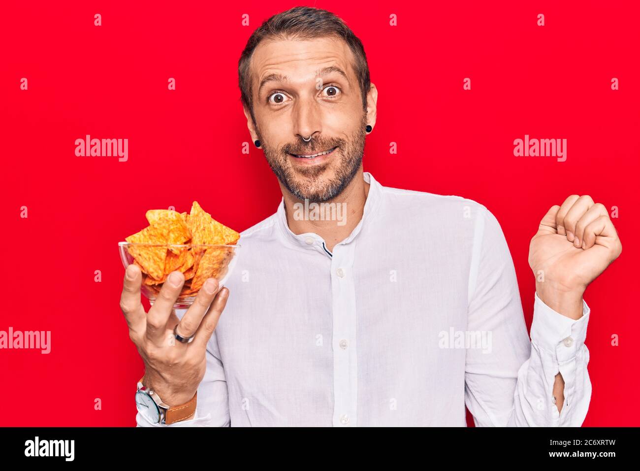 Young handsome man holding nachos potato chips screaming proud ...