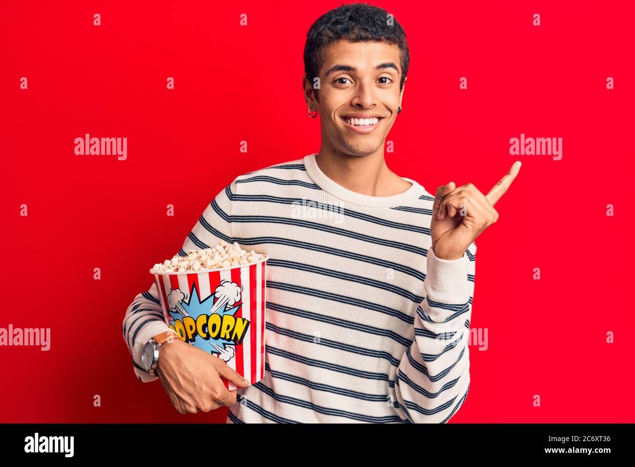 Young african amercian man holding popcorn smiling happy pointing with hand and finger to the ...
