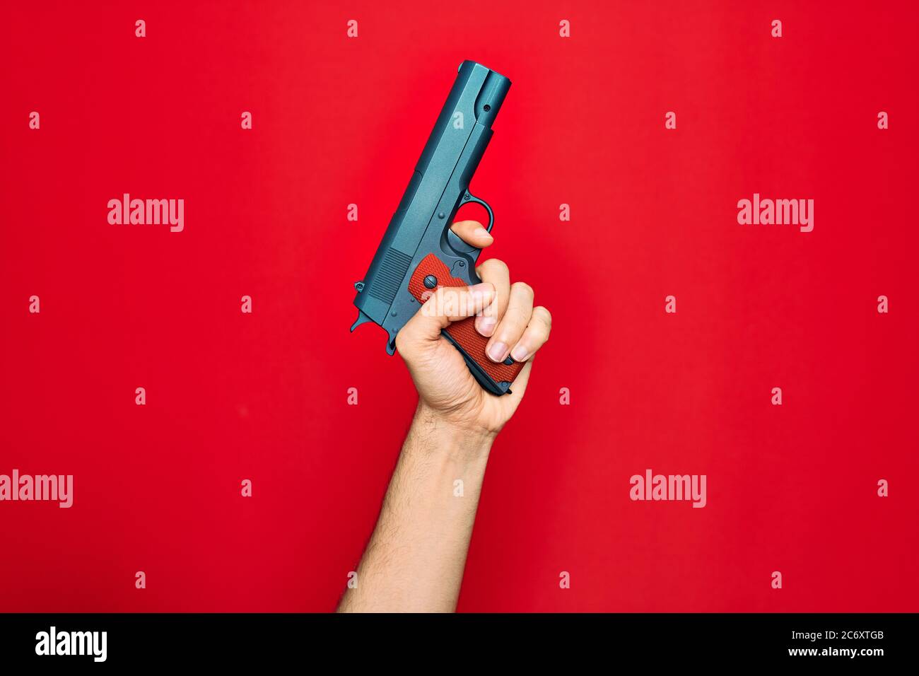 Beautiful hand of man holding gun over isolated red background Stock ...