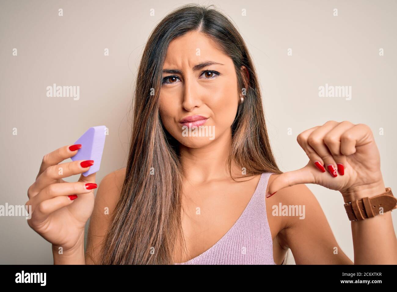 Young beautiful woman using beauty sponge with facial makeup over pink ...