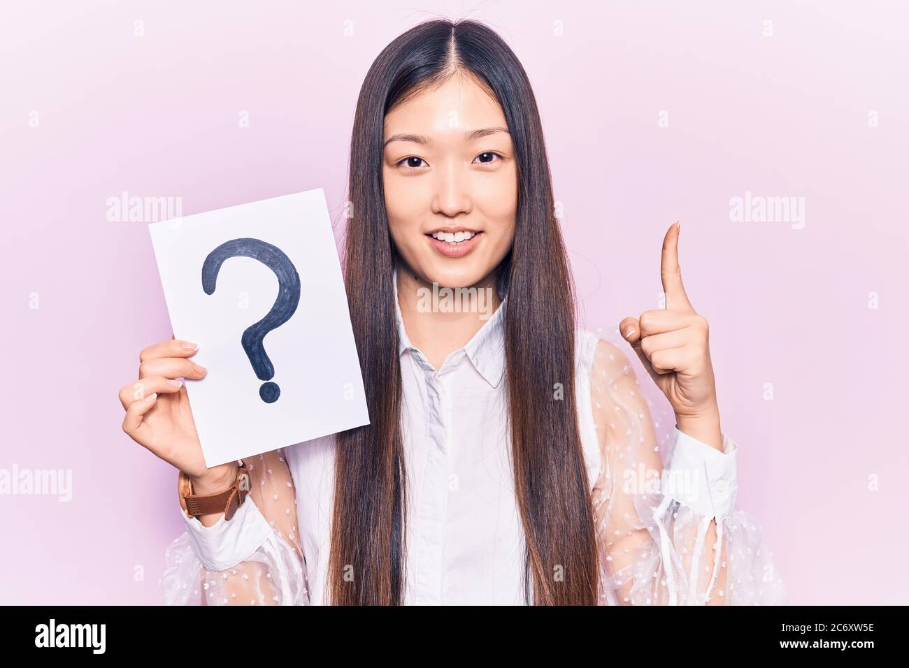 Young beautiful chinese woman holding question mark smiling with an ...