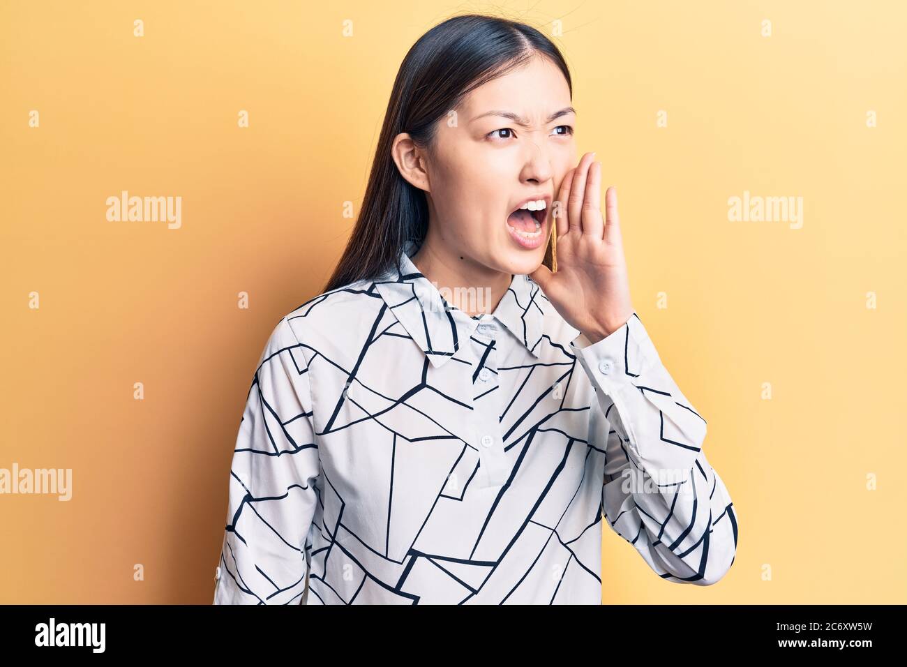 Young beautiful chinese woman wearing elegant shirt shouting and ...