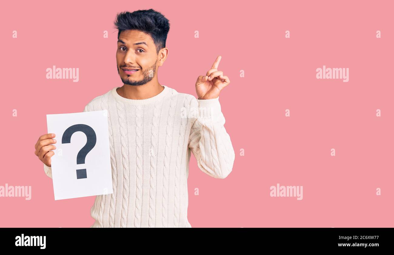 Handsome latin american young man holding question mark surprised with ...
