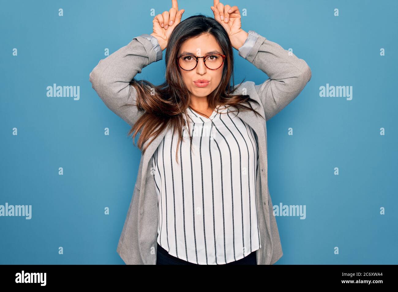 Young hispanic business woman wearing glasses standing over blue ...