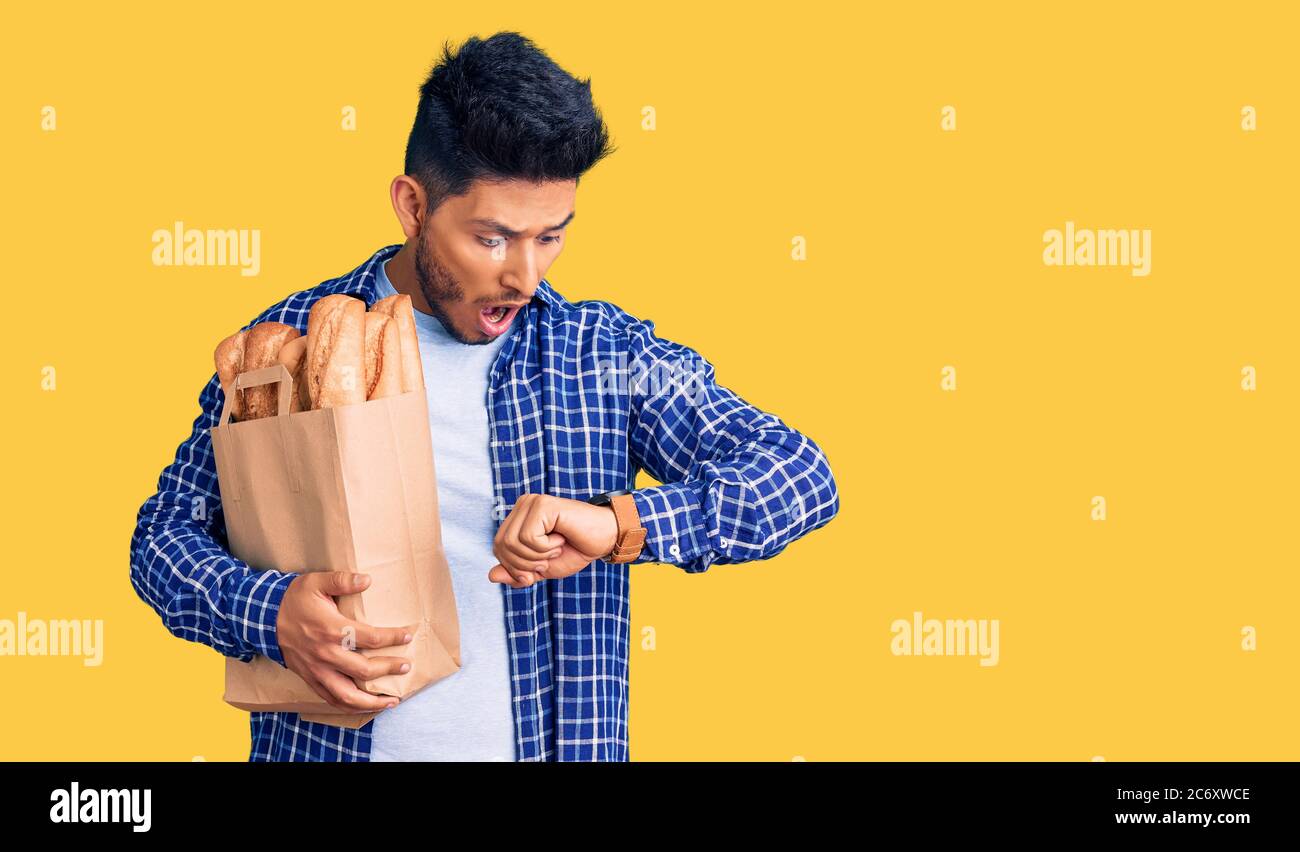 Handsome latin american young man holding paper bag with bread looking ...