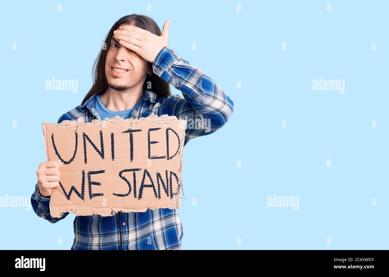 Young adult man with long hair holding united we stand banner stressed ...
