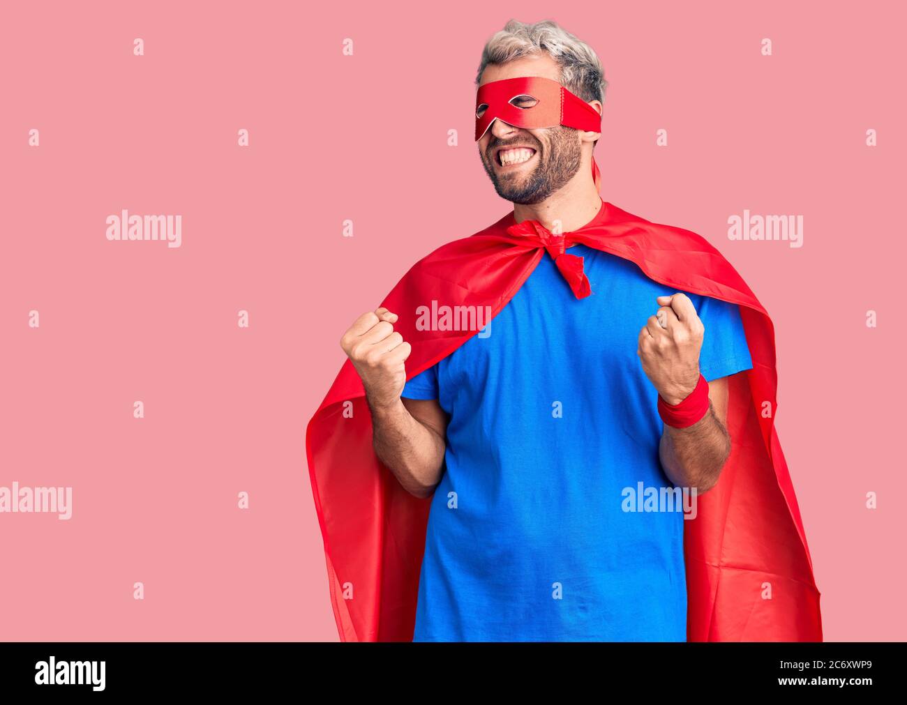 Young blond man wearing super hero custome excited for success with ...