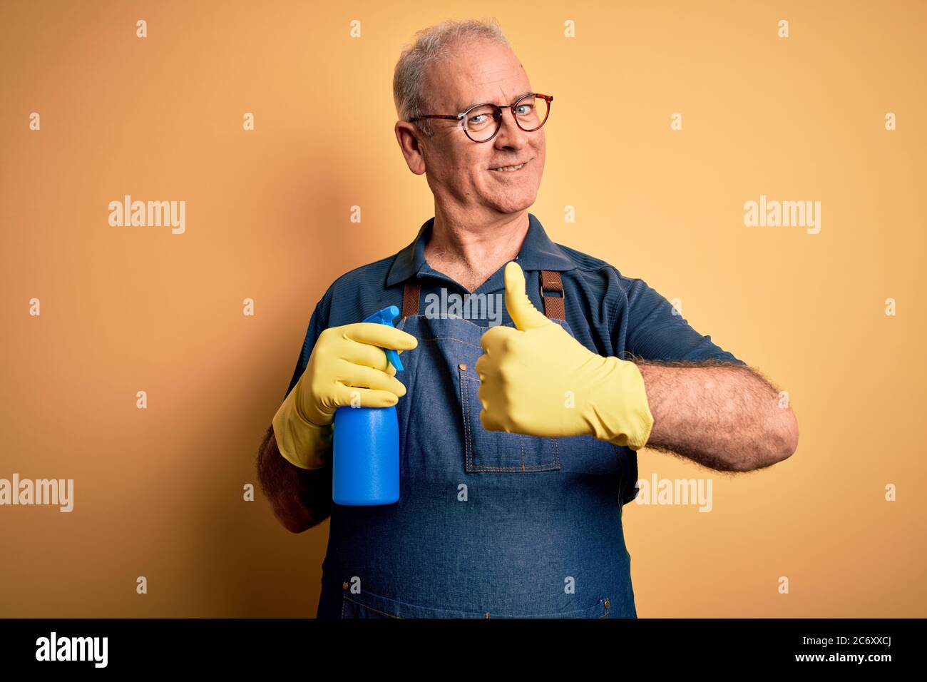 Middle age hoary cleaner man cleaning wearing apron and gloves using ...