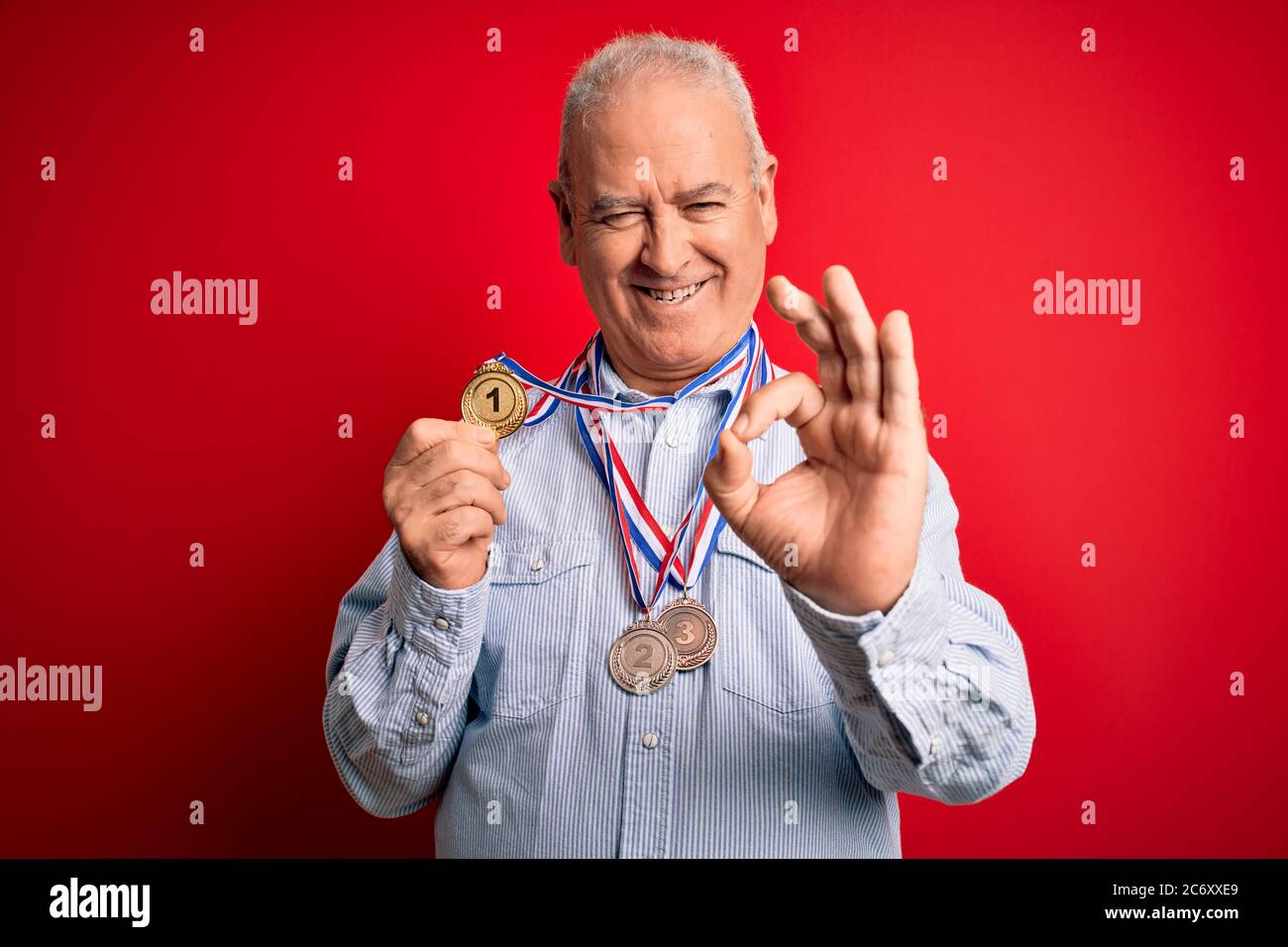 Middle age hoary champion man wearing medals standing over isolated red ...