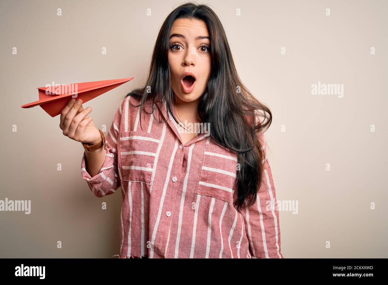 Young brunette woman holding origami paper plane over isolated ...