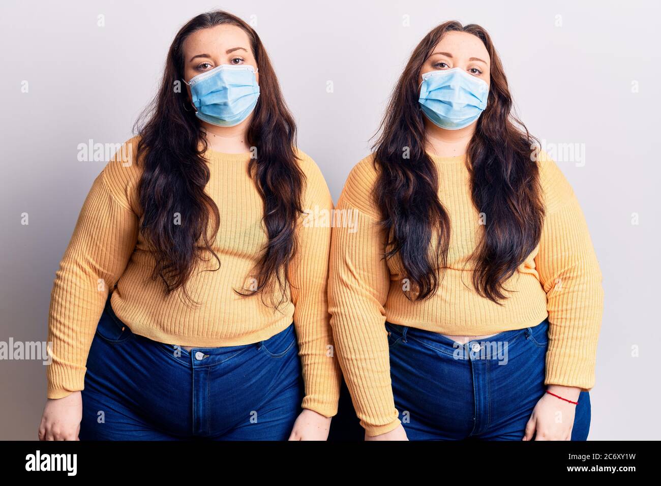 Young plus size twins wearing medical mask relaxed with serious ...