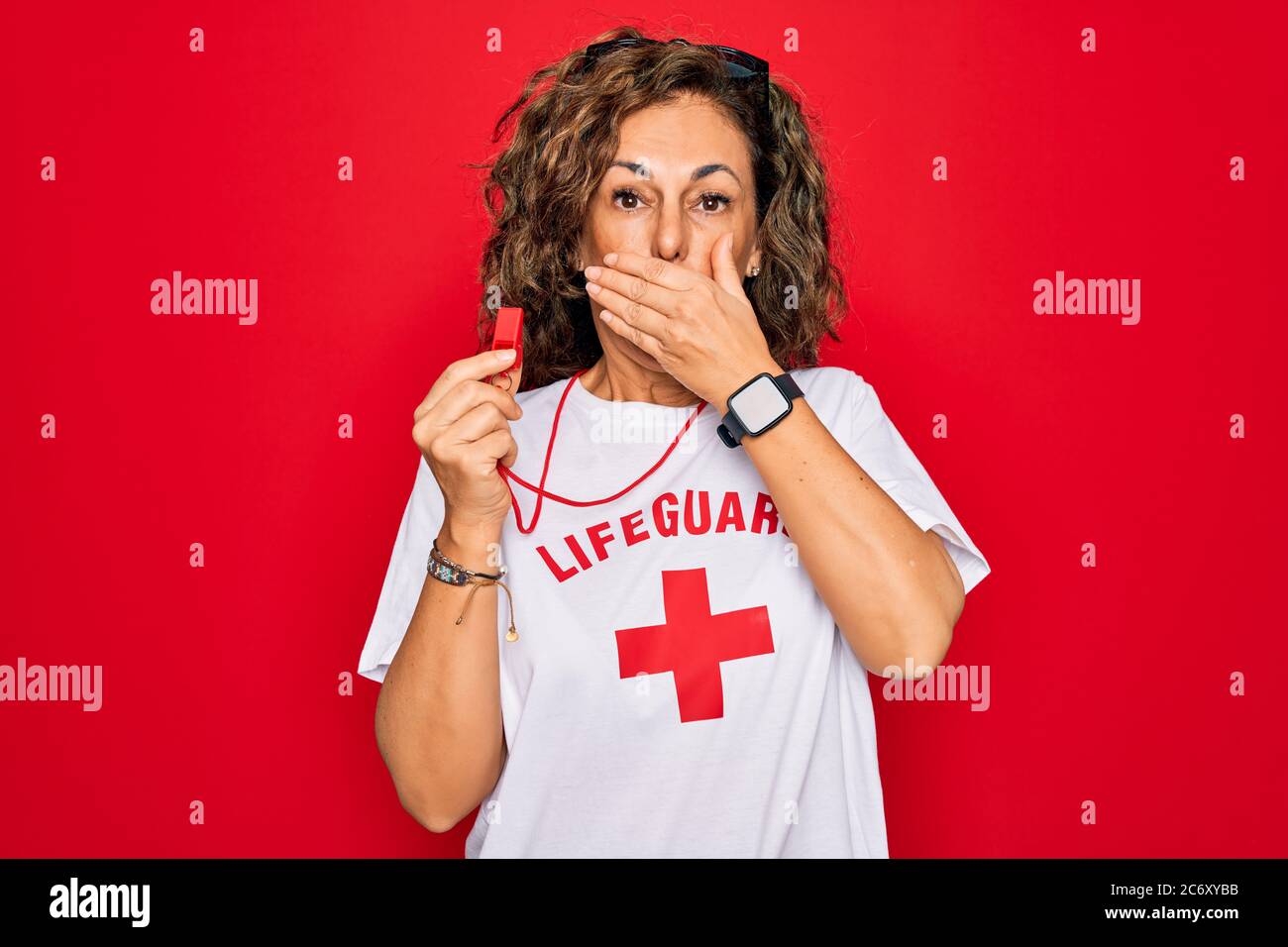 Middle age senior summer lifeguard woman holding whistle over red ...
