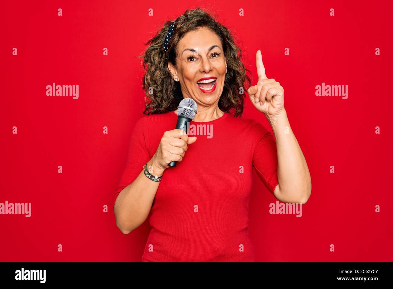 Middle age senior singer woman singing using music microphone over red ...