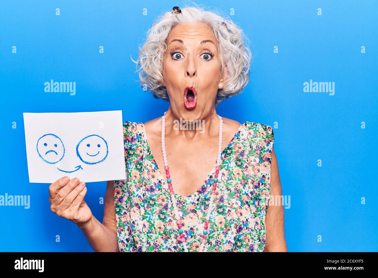 Senior grey-haired woman holding sad to happy emotion paper scared and ...