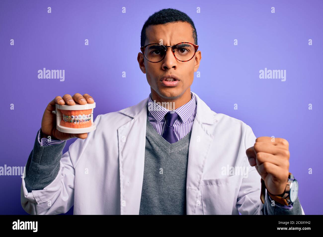 Young handsome african american dentist man holding denture teeth with ...