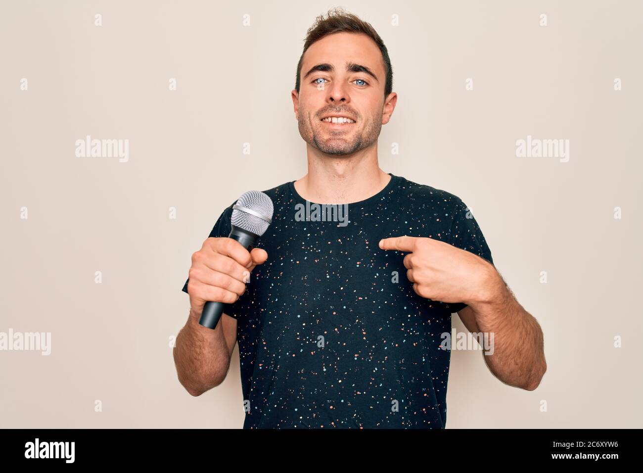 Young handsome singer man with blue eyes singing using microphone over white background with ...