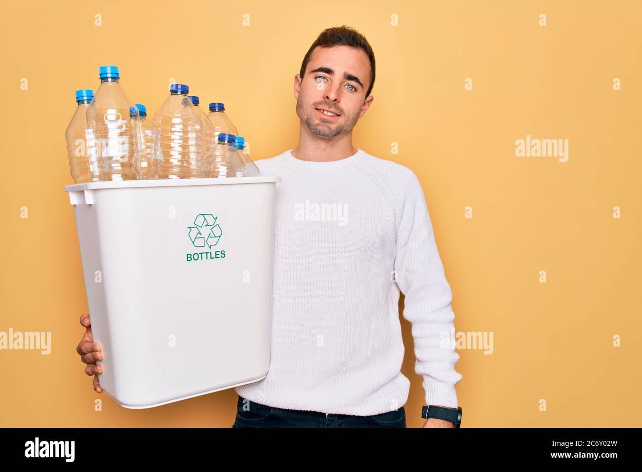 Young handsome man with blue eyes recycling holding wastebasket with ...