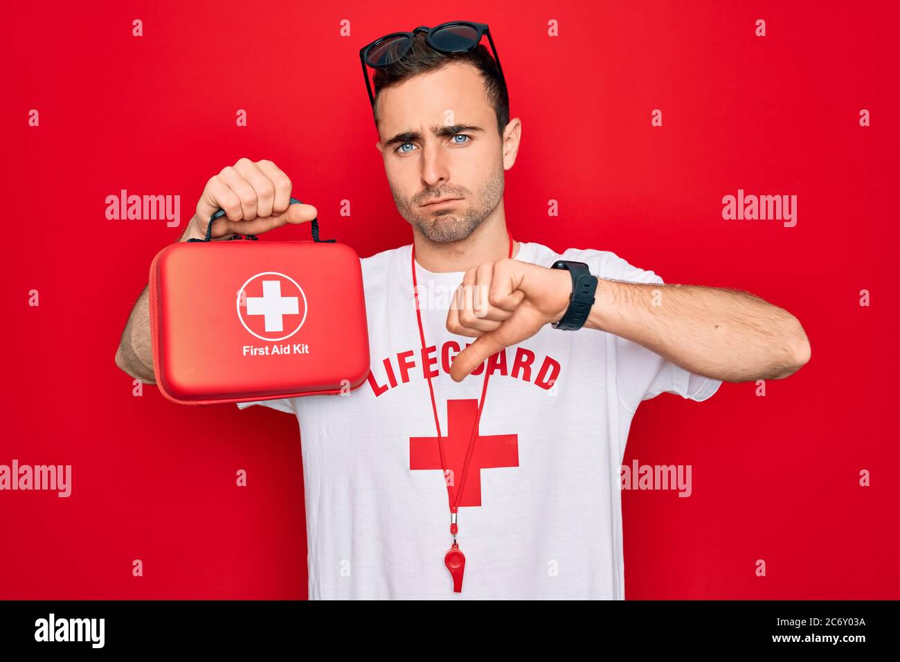 Young handsome lifeguard man wearing t-shirt with red cross and whistle ...