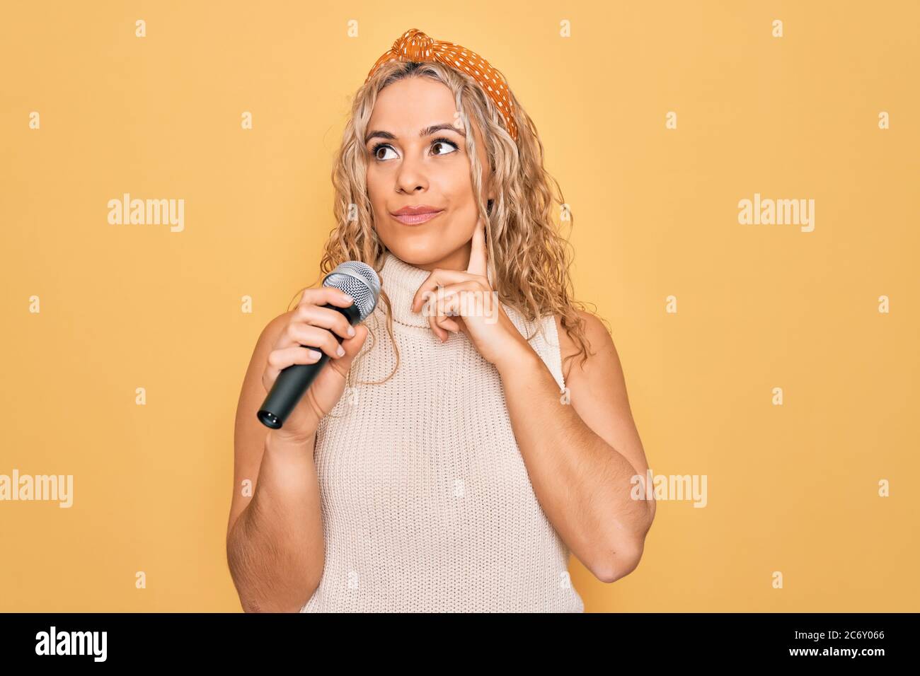 Young beautiful blonde singer woman singing using microphone over ...
