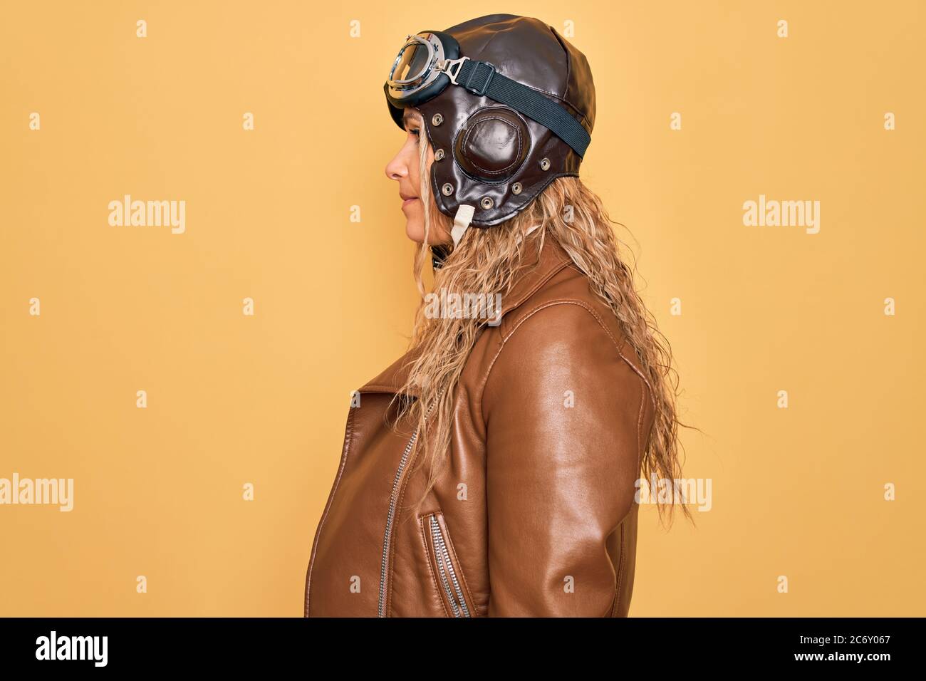 Young beautiful blonde aviator woman wearing vintage pilot helmet whit ...