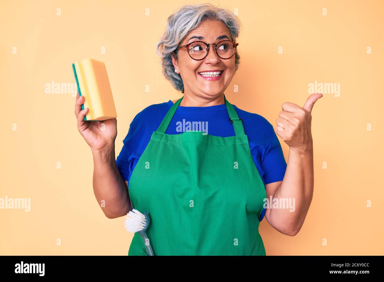 Senior hispanic grey- haired woman wearing apron holding scourer ...