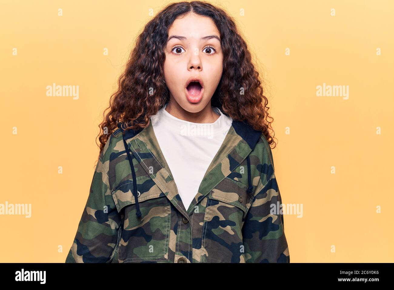 Beautiful kid girl with curly hair wearing camouflage jacket scared and ...