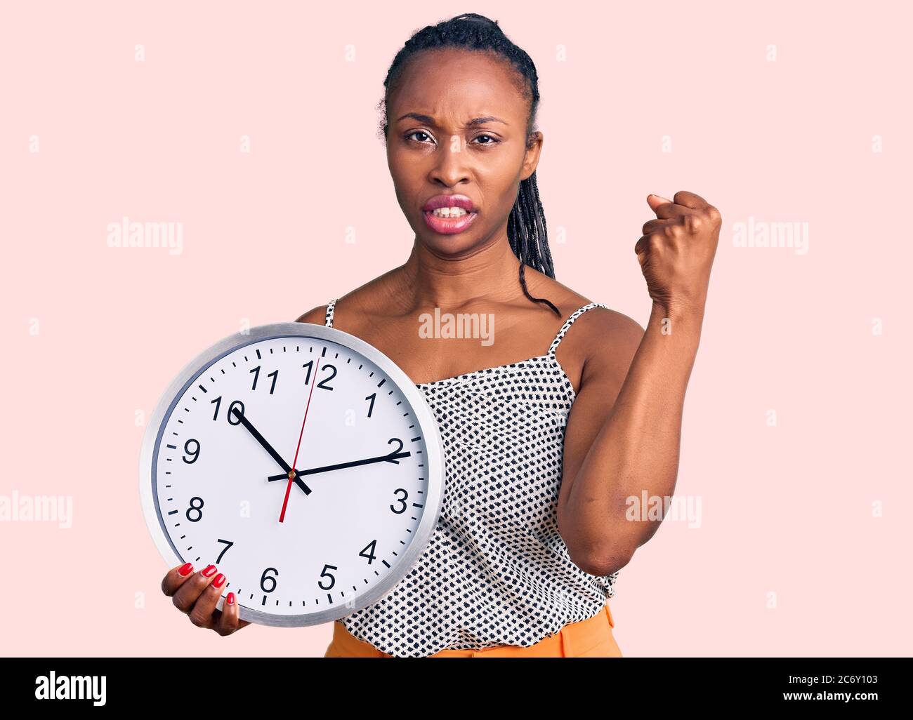 Young african american woman holding big clock annoyed and frustrated ...