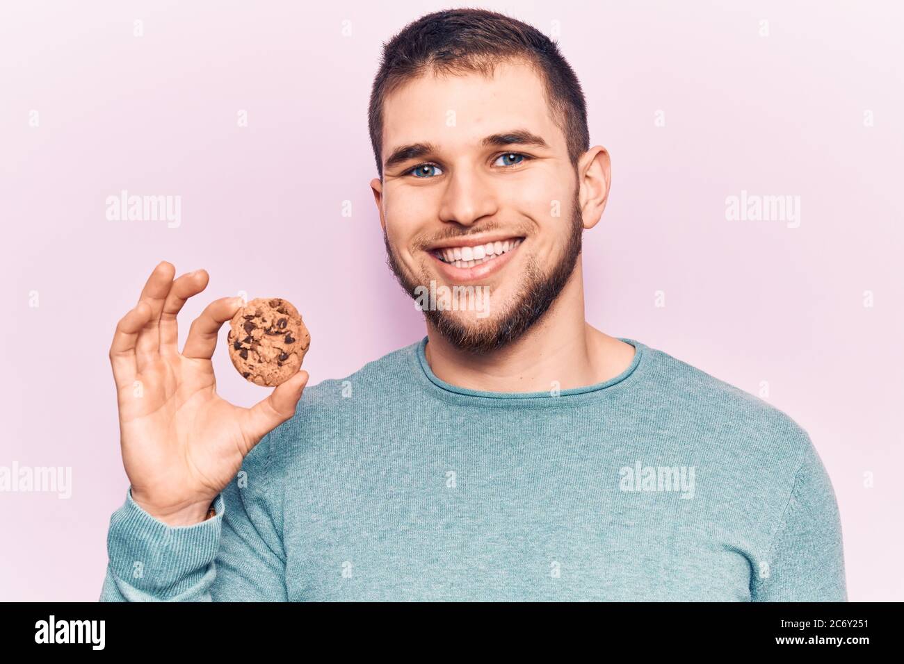 Young handsome man holding cookie looking positive and happy standing ...
