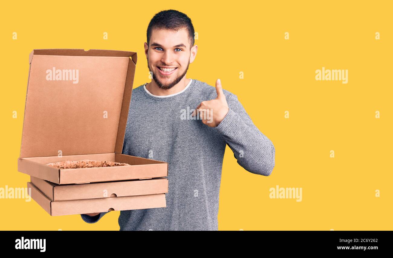 Young handsome man holding delivery italian pizza boxes pointing finger ...
