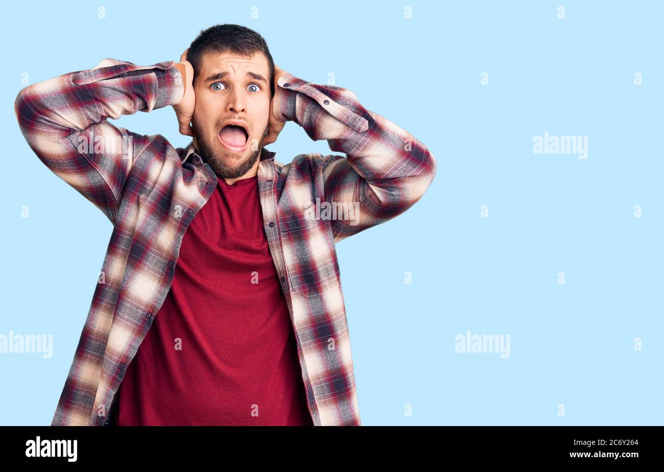 Young handsome man wearing casual shirt crazy and scared with hands on ...