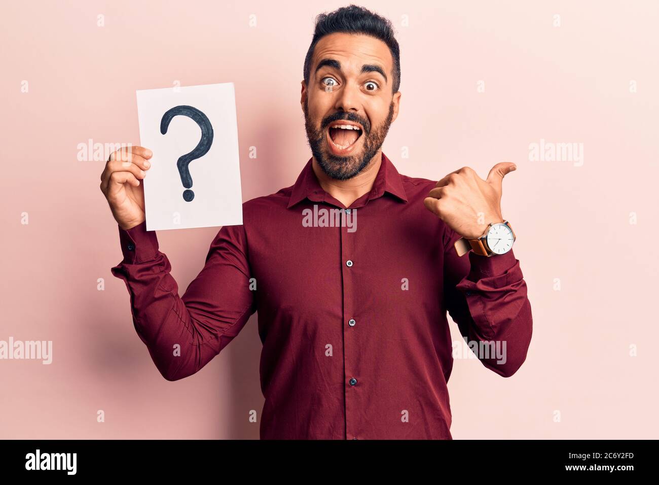Young hispanic man holding question mark pointing thumb up to the side ...