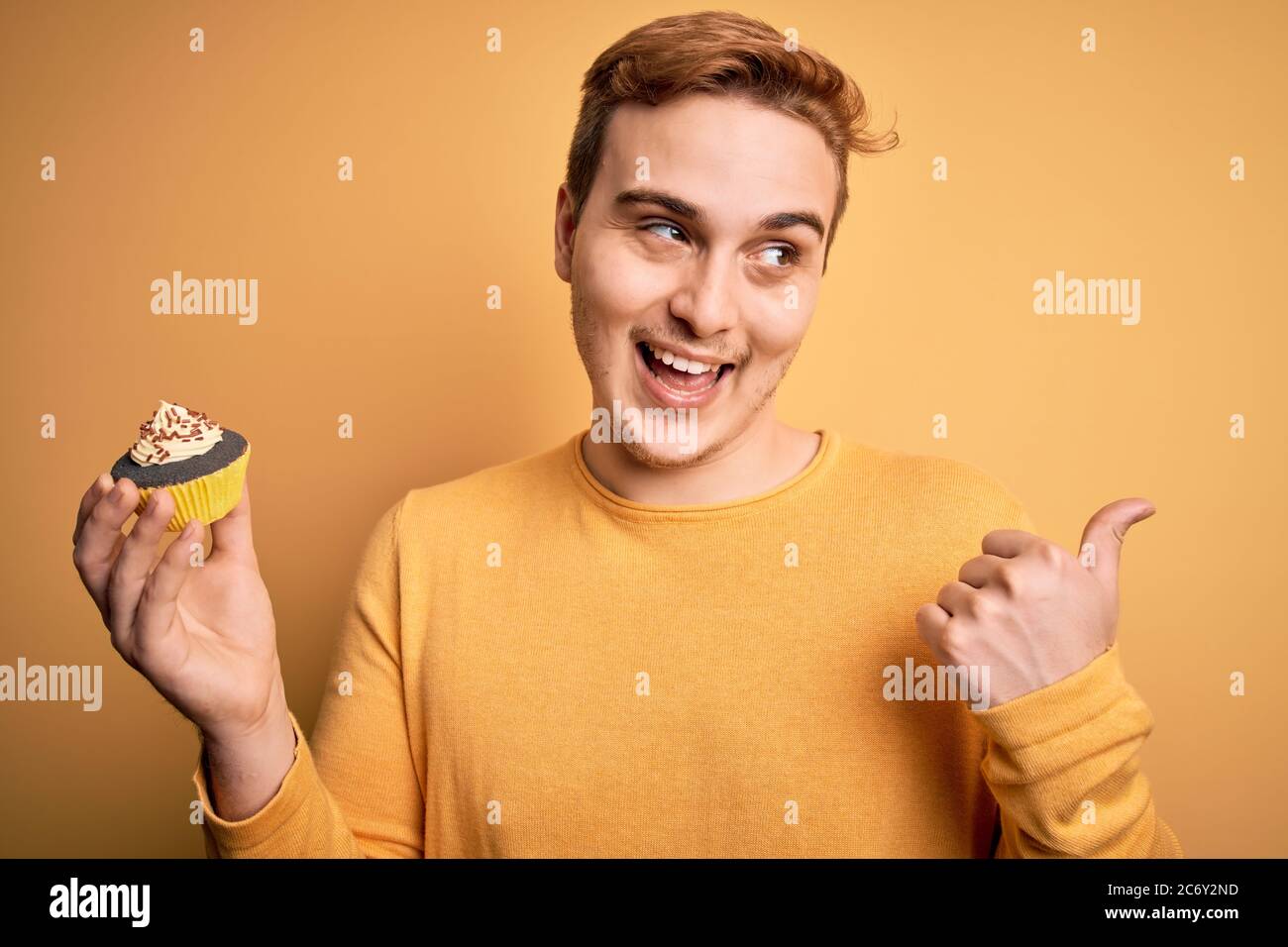 Young handsome redhead man eating sweet chocolate cupcake dessert over ...