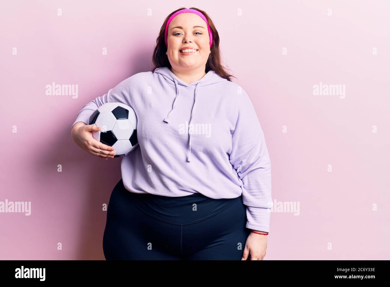 Young plus size woman holding soccer ball looking positive and happy ...