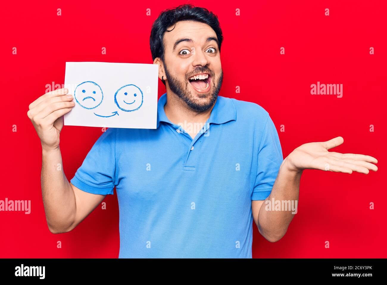 Young hispanic man holding sad to happy emotion paper celebrating ...