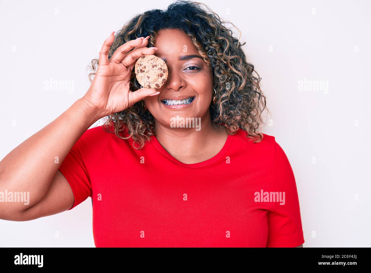 Young african american plus size woman holding cookie looking positive ...