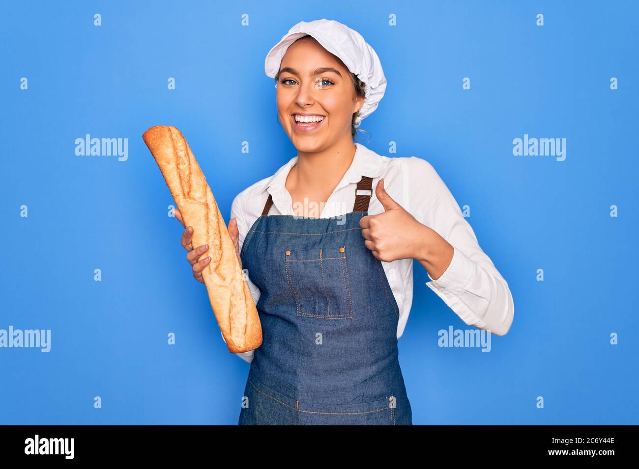Young beautiful blonde baker woman with blue eyes holding loaf of ...