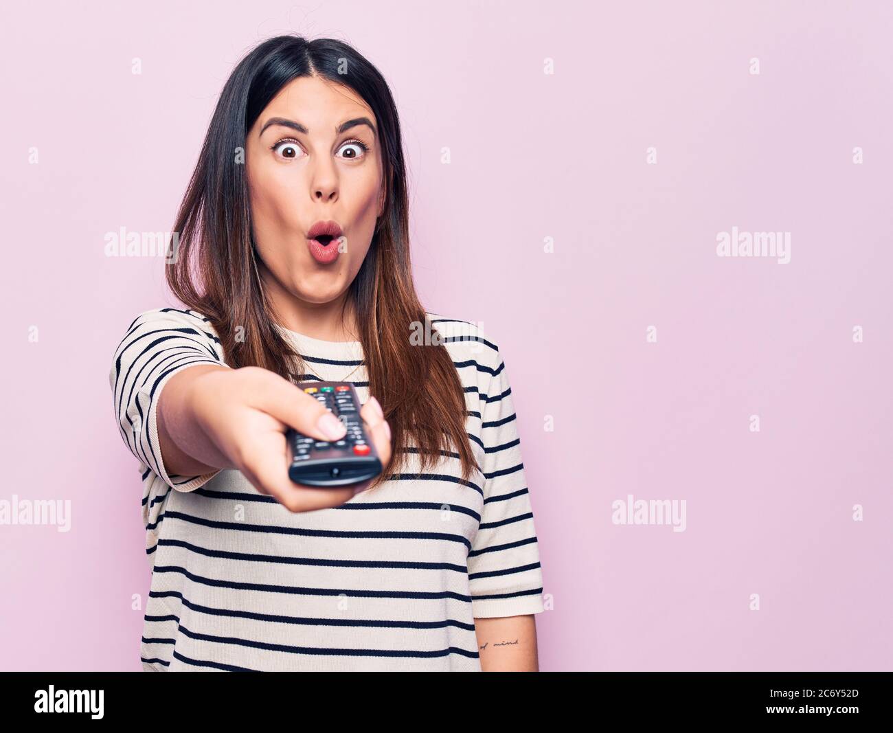 Young beautiful brunette woman holding television remote control over ...