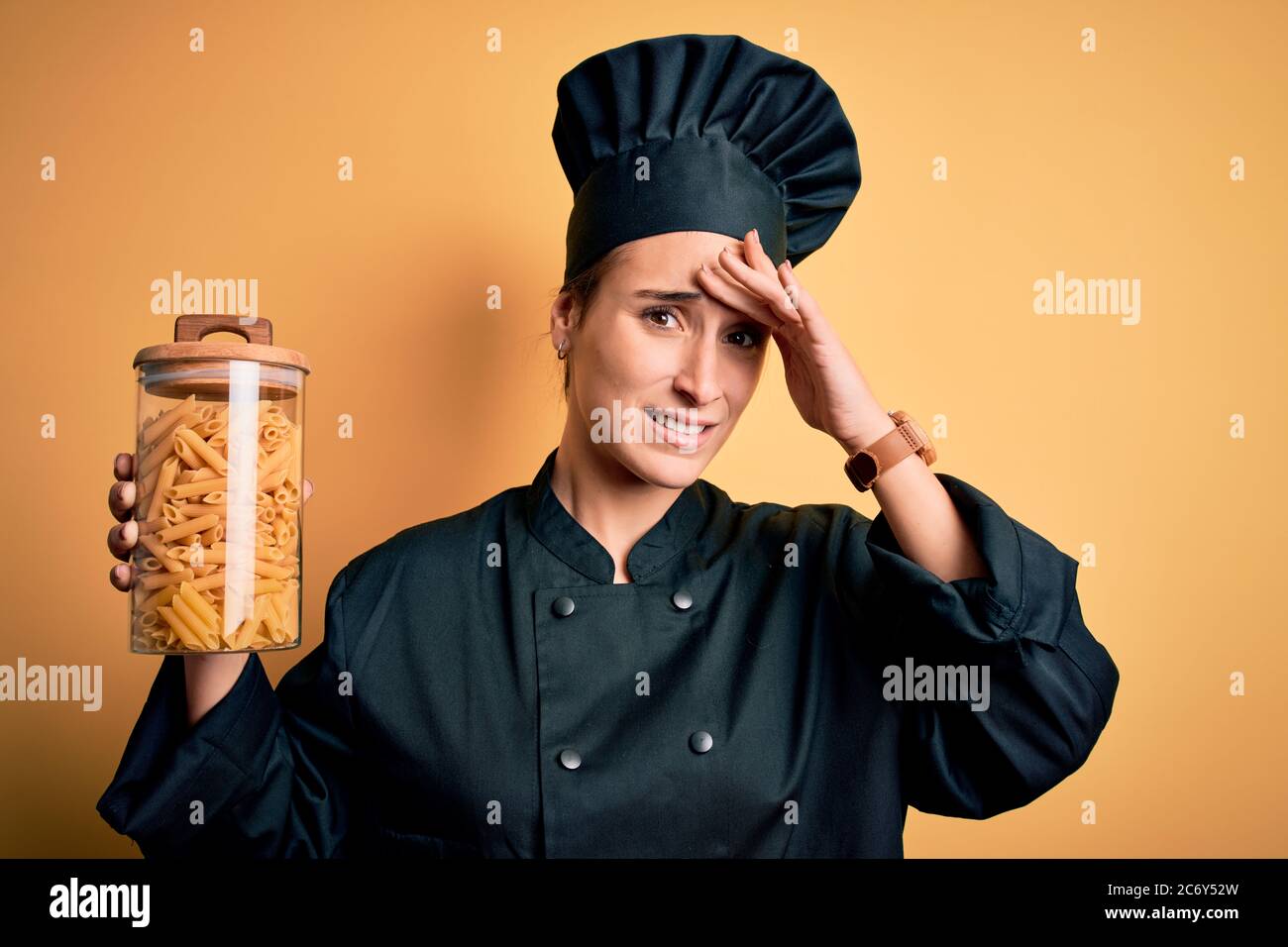 Young beautiful chef woman wearing cooker uniform holding jar with ...